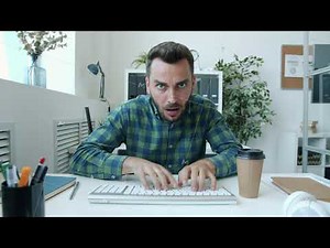 Mad office worker typing drinking coffee in hurry then throwing keyboard at camera