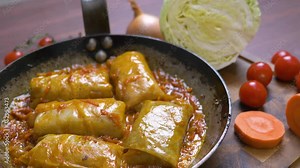 A pan with cooked cabbage rolls stands on a cutting board. Tomato sauce boils in a pan with cabbage rolls. Cooking cabbage rolls. Cabbage rolls under tomato sauce. Hand held studio shot