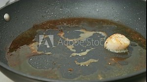 Close-up frying Raw Sea Scallops into a pan with oil on a gas stove in 4K. Concept of cooking scallops with salt and pepper, flipping around, and checking for a well-done cook in slow-motion.