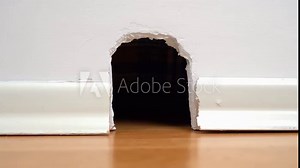 A hole in white wall, drywall, cut hole, gnawed mouse shelter, entrance to the housing of rodent, rat Close-up Damage to the baseboard, cable hole, repair, dismantling The pest chewed a hole in house