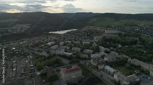 10. Aerial view of city with low buildings. Cars are driving. in the frame garages, school, lake. In the background are the Ural mountains. Summer, evening. Russia, Satka city