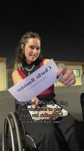 one of my DREAM roles i am so excited 🥹 i think little reds story works so well being a mobility aid user and i am so excited to share it with the world!!! let me know your takes/opinions in the comments! [alt text: charlie is wearing a black tank top and pants and a red tank top over their black top, hair half up half down, sitting in their black wheelchair. they spin in a wheelie smiling and lip syncing then hold up an “into the woods” script, pulling out their name card. text on screen reads