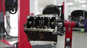 Auto mechanic works on car engine overhaul in modern garage. Disassembled engine block, crankshaft, rod bearings exposed, restoration process captured. Vehicle maintenance, mechanical service shop.