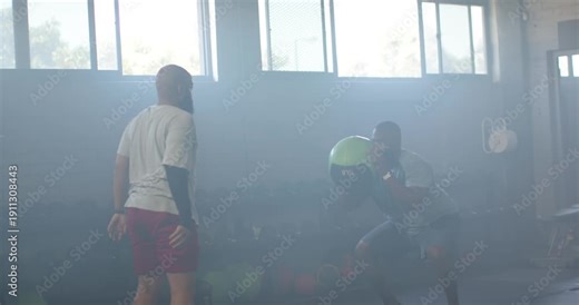 Two African American men picking green med ball tossing, catching and squatting for training in gym