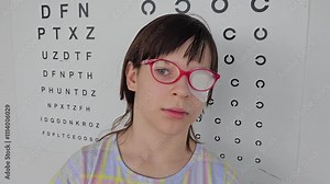 Child with eye patch and glasses in front of eye exam chart at medical clinic
