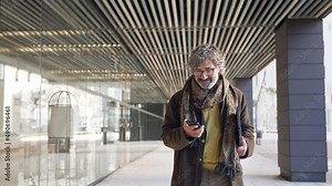 Senior professional stylish business man checking cell phone message app while walking outside the office