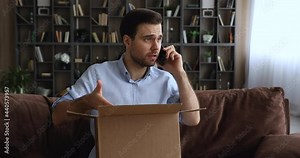 Man sitting on sofa with opened parcel express complaints to seller or courier on the phone about damaged goods, crashed items inside cardboard box. Dissatisfied e-commerce customer, claims concept