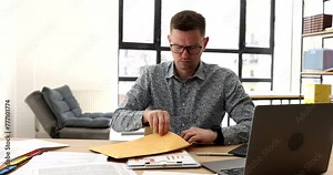 Businessman sorting mail at table and opening yellow envelope in office. Sending invoices by post concept