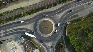 Aerial drone Top Down Pedestal down footage of cars and trucks driving around a roundabout intersection merging and switching lanes. Industrial traffic on an european road. Solar panel light.