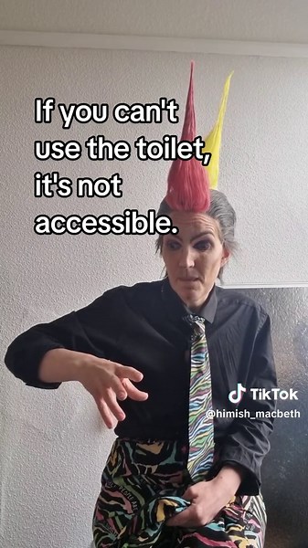 Disabled people need to pee, too. (And we're not too mature to giggle at 'backlog' in the context of a discussion about toilets.) Video description: Video is of me, a white drag king in my 40s, wearing a rainbow mohawk and zebra patterned suit, both in the colours of the disability pride flag. Full transcript: