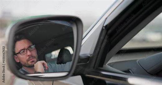 Reflection in car side view mirror - Young Caucasian man sits in a car on a parking lot and looking forward