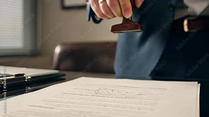 Businessman stamping approval on official document with wooden stamp at office desk.