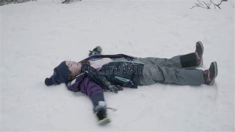 A Young Girl Makes A Snow Angel By Lying On Her Back In The Snow And Moving Her Arms And Legs
