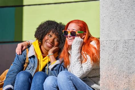 Dos Chicas Lesbianas Sentadas Abrazadas Una Blanca Con Cabello Naranja Y La Otra Negra Con