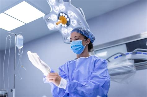 Retrato De Una Hermosa Doctora Cirujana Poniéndose Guantes Médicos De Pie En El Quirófano