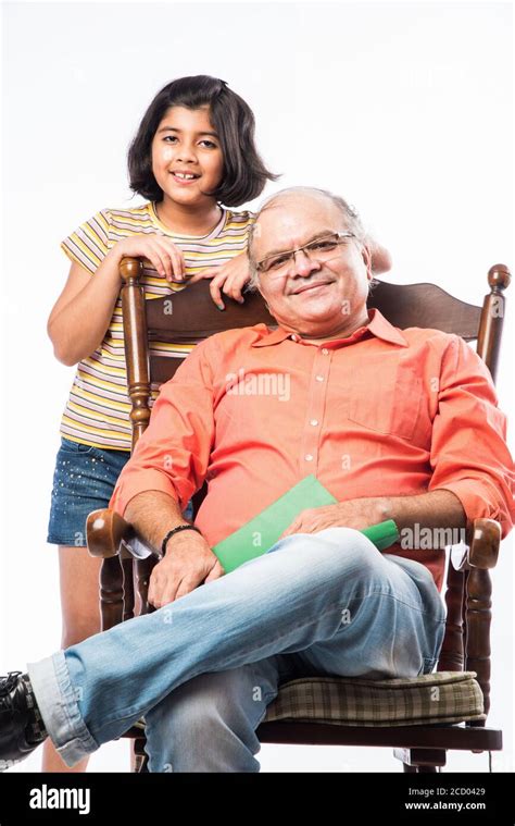 Indian Senior Man Or Grandpa Reading Book With Granddaughter Or Grand Daughter While Sitting On