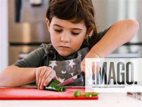 Focused Girl With Brown Hair And In Apron Slicing Fresh Green Pepper On Kitchen Counter While