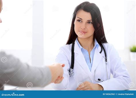 Brunette Female Doctor Shaking Hands With Patient During A Conversation With Her Stock Image