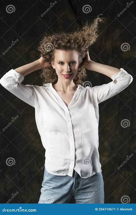 A Beautiful Girl Wearing Jeans And A Blouse Poses Cheerfully In The Wind Which Blows Her Long