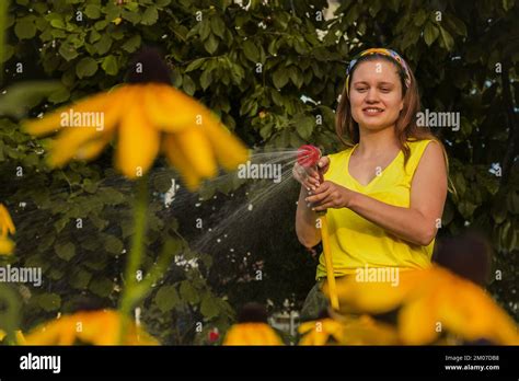 Young Pretty Girl Having Fun In The Garden Watering Plants With A Hose Smiling While Taking A