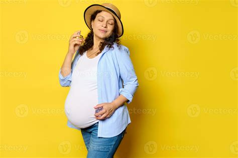 Portrait Of A Beautiful Curly Haired Pregnant Woman Putting Hand On Her Belly Applying Perfume