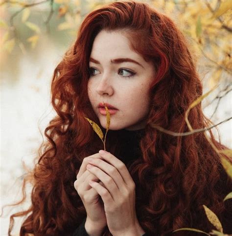 A Woman With Long Red Hair Holding A Leaf In Her Hand And Looking At The Camera