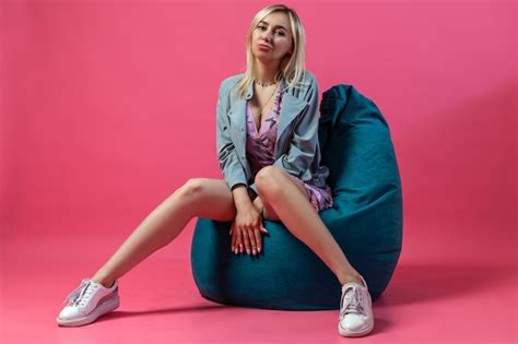 Premium Photo Beautiful Blonde Girl In A Blue Jacket Sits On A Green Bag Chair With Her Legs
