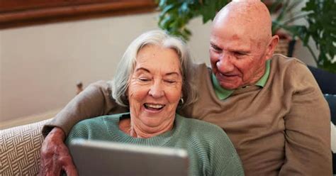 Senior Couple Tablet And Laugh In Home While Reading Social Media Post News App And Ebook On
