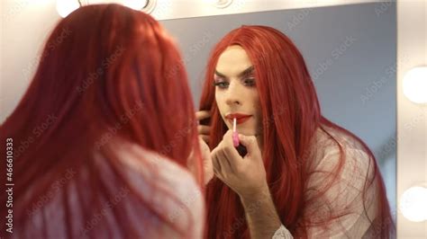 Confident Transgender Woman In Red Wig Applying Red Lipstick Reflecting In Mirror Portrait Of