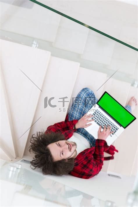 穿着浴袍的年轻自由职业者坐在楼梯上使用笔记本电脑在家工作领带头饰高清摄影大图 千库网
