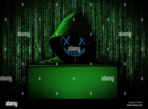 hacker with glowing mask behind notebook laptop in front of green source binary code background
