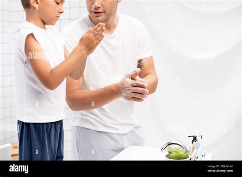Father And Son Rubbing Soap Between Hands While Standing Near Sink In