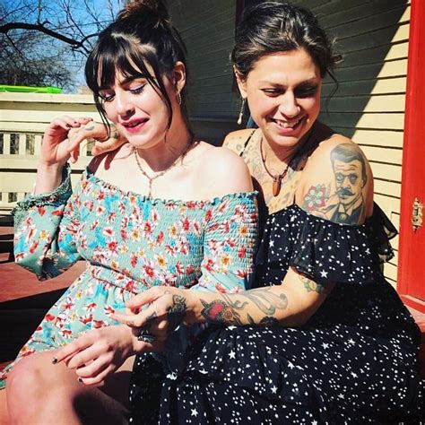 Two Women Sitting On A Porch With Their Arms Around Each Other And One Woman Has Tattoos On Her Arm