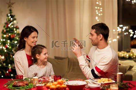 假期家庭和庆祝活动的概念 快乐的母亲父亲和小女儿在家里吃圣诞晚餐并用智能手机拍照高清摄影大图 千库网