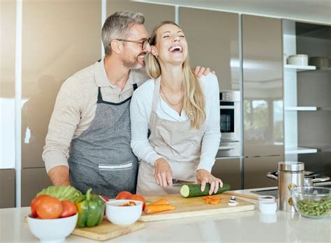 Couple In Kitchen Cooking Together In Their Home Having Fun And Laughing Middle Aged Man And