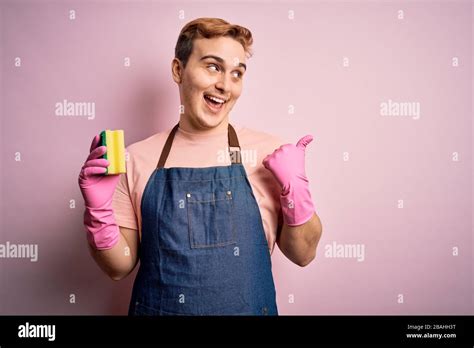 Handsome Redhead Man Doing Housework Wearing Apron And Gloves Using Cleaner Scourer Pointing