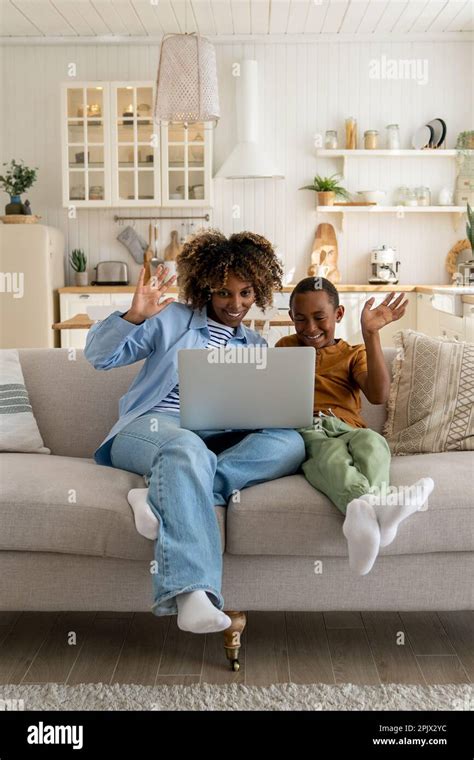 Happy Cheerful African American Mother And Son Sit On Sofa With Laptop