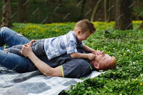 Free Photo Cheerful Dad And Son Have Fun Playing On The Plaid In A Green Park