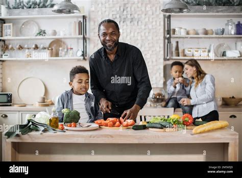 Handsome African Father And Son Preparing Tasty Salad At Kitchen While