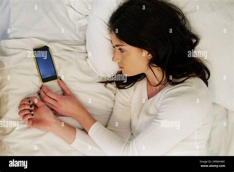 Shes Still Waiting For His Calla Young Woman Lying In Bed While Looking At Her Cellphone